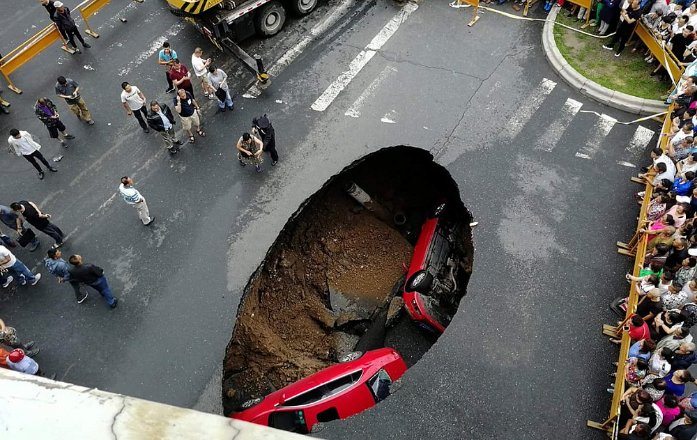Massive sinkhole swallows two cars with three people inside
